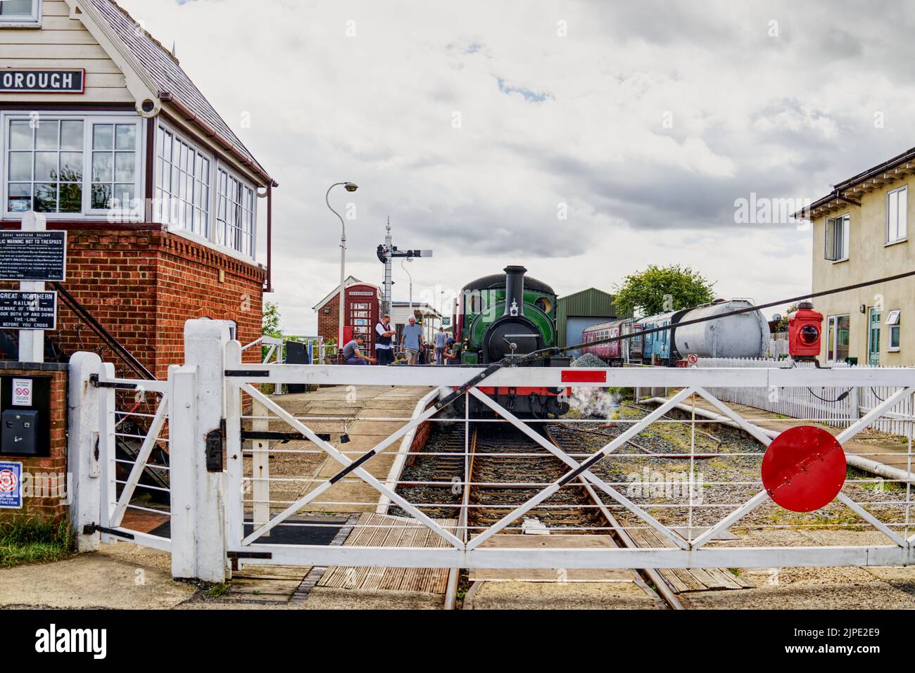 Steam train at platform viewed across level crossing gate in railway ...