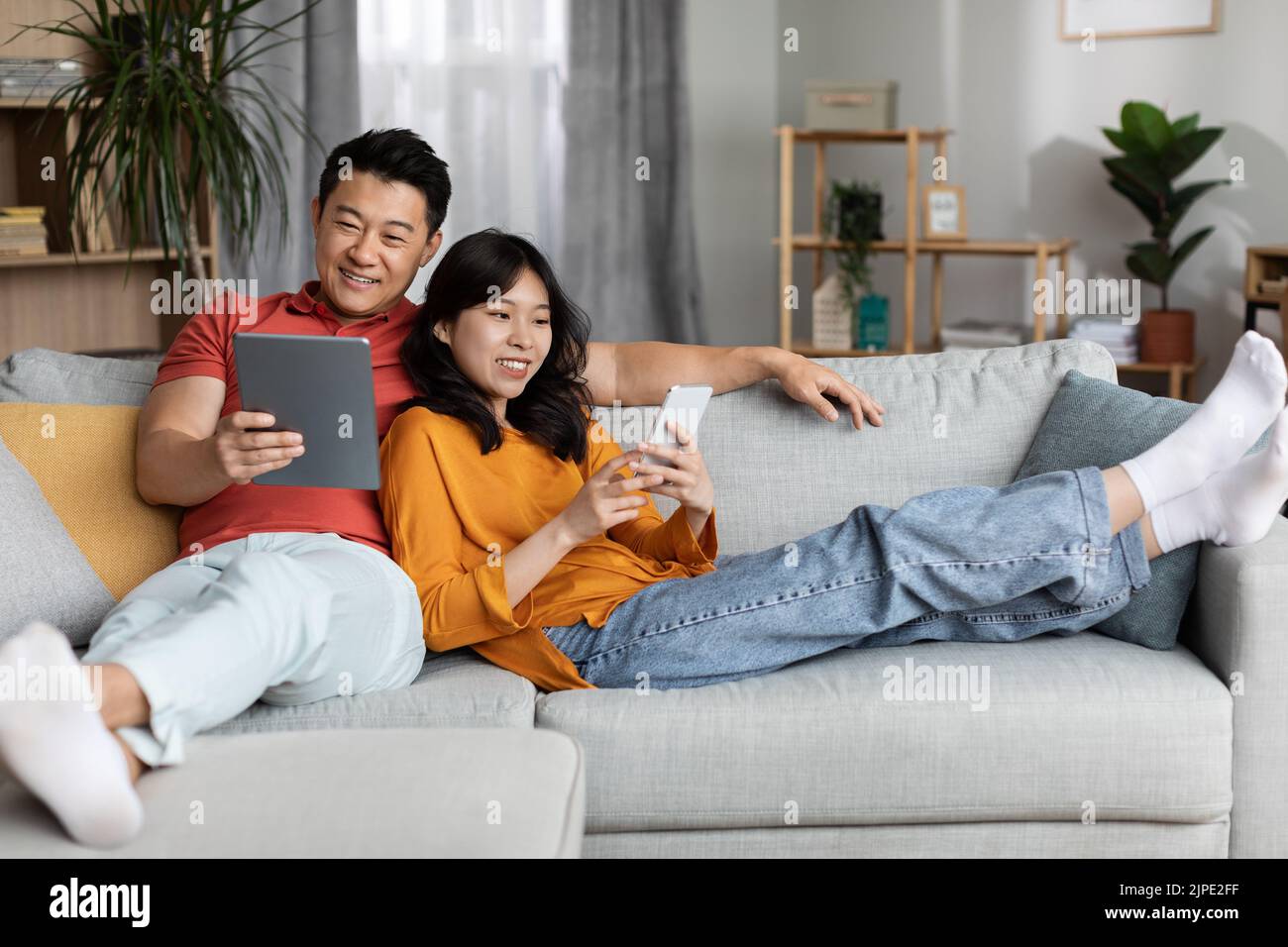 Relaxed asian couple chilling together at home, using gadgets Stock ...
