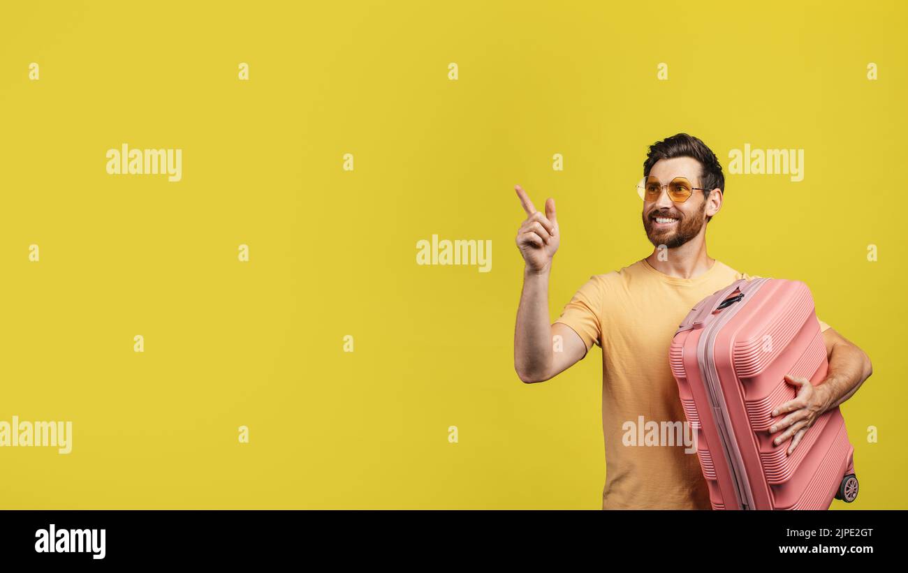 Happy man holding suitcase and pointing at free space over yellow ...