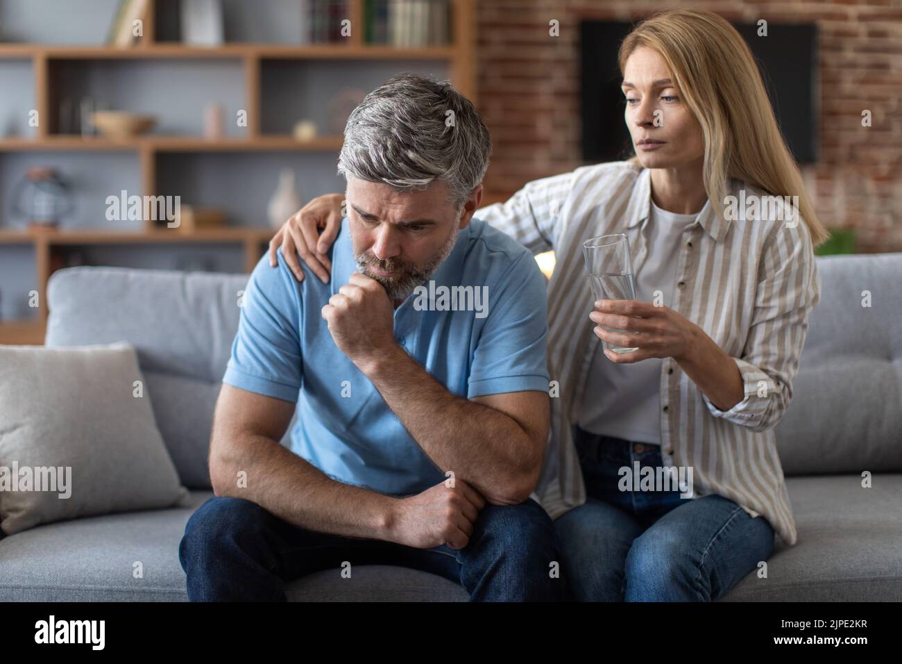 Upset adult caucasian wife calm husband, gives glass of water, man ...