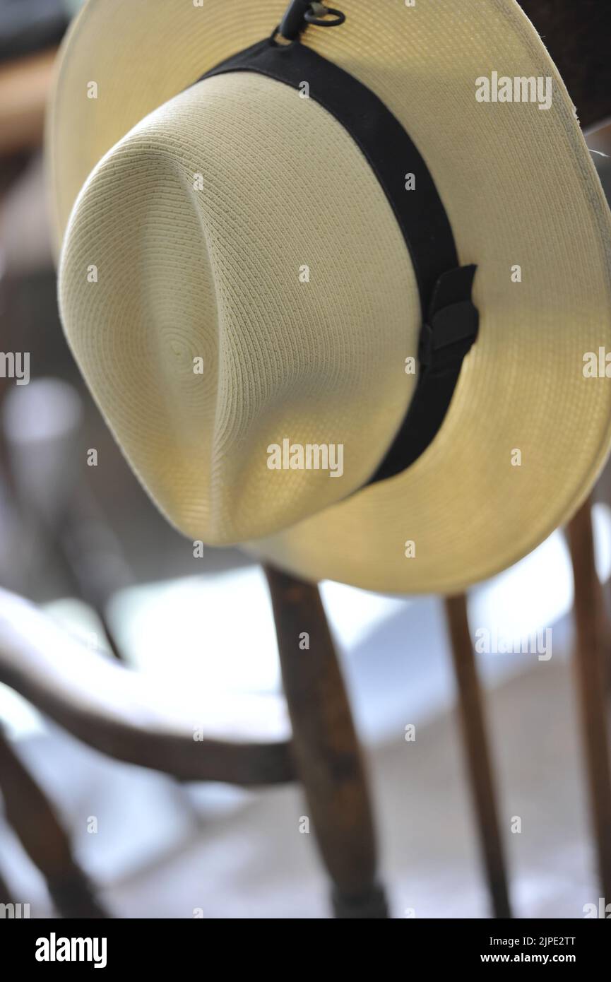 Mans hat with black band hanging on the back of a ladder back wooden ...