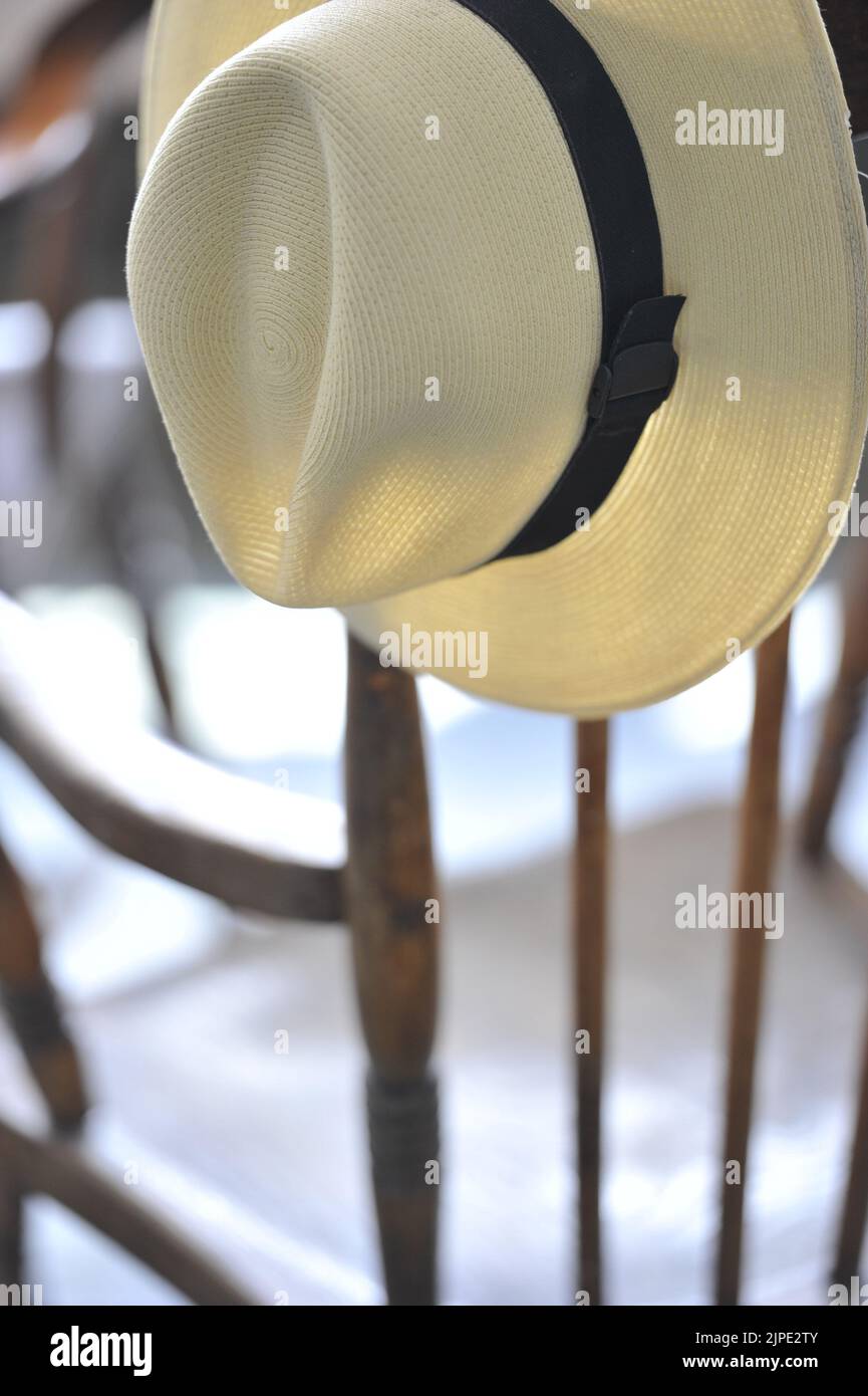 Mans hat with black band hanging on the back of a ladder back wooden ...