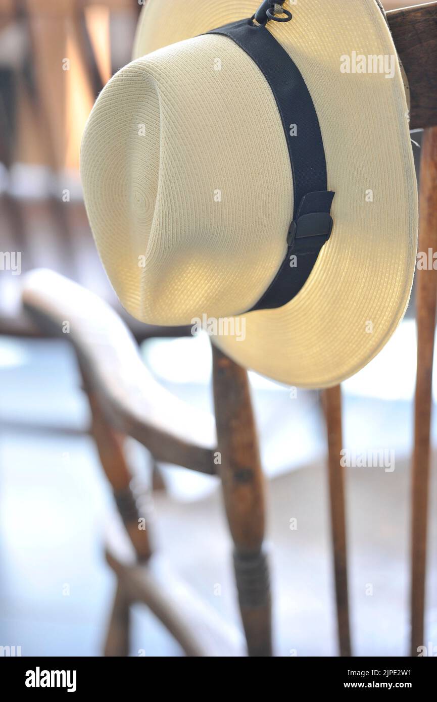 Mans hat with black band hanging on the back of a ladder back wooden ...