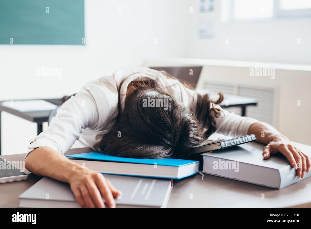 Tired female student sleeping on desk face and hands on books Stock ...