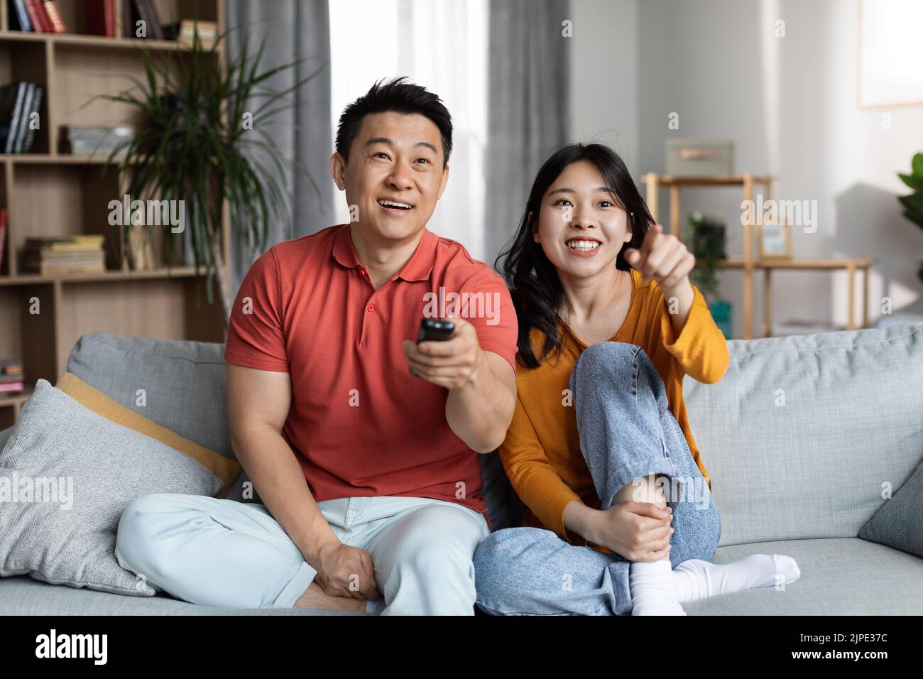Happy asian man and woman watching TV at home Stock Photo - Alamy
