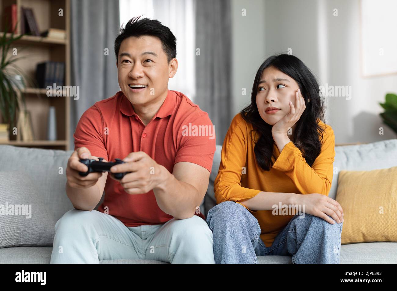 Bored asian woman sitting by her boyfriend playing video games Stock ...