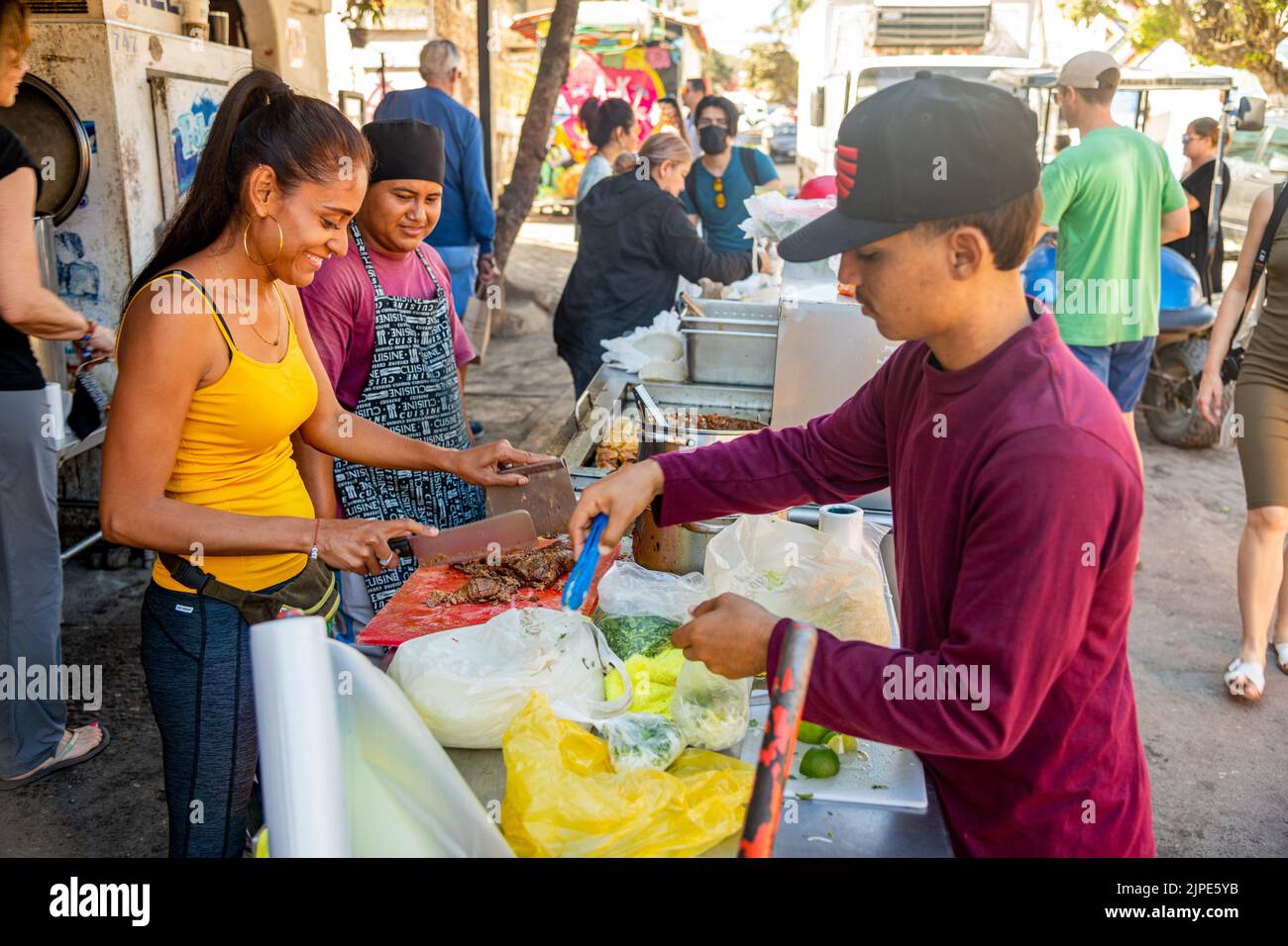 A woman chopping meat in preparation for tacos at a street food stall ...