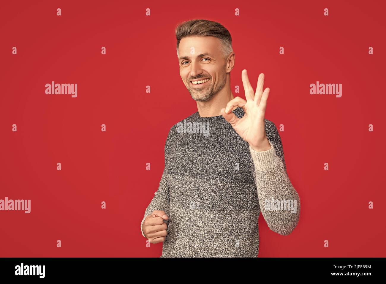 smiling grizzled guy in sweater on red background show ok gesture ...