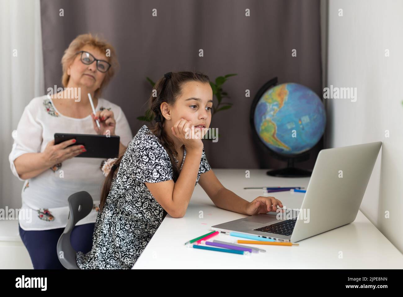 Older woman grandma and little girl grandkid with homework remote study ...