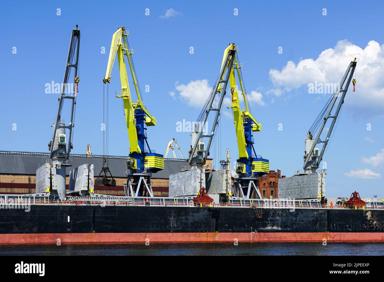 Yellow and blue painted cranes load coal into a bulk carrier in the ...