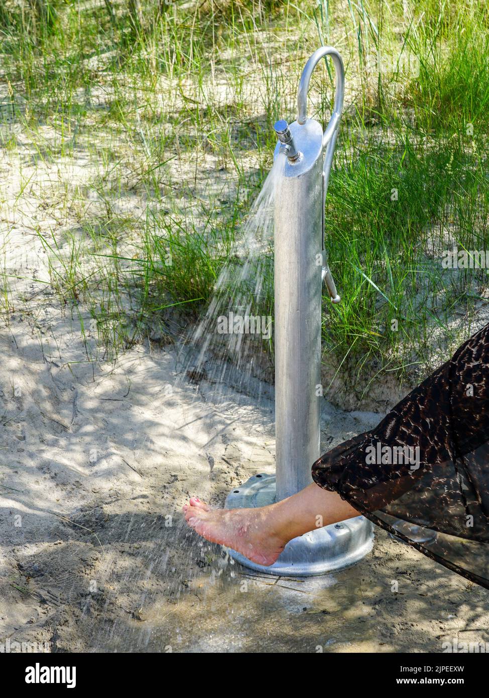 Woman removing sand from his legs under beach shower near sandy dune ...