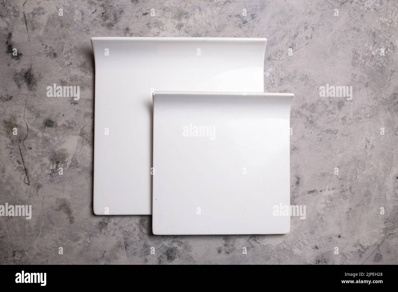 white ceramic square plates on a concrete background Stock Photo - Alamy