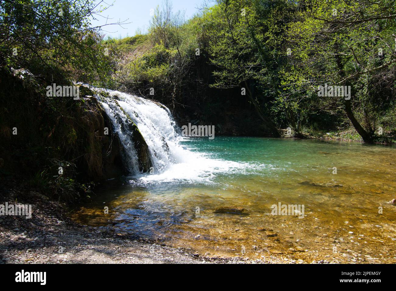 The waterfall flowing to the river in the forest of Marche on a sunny ...