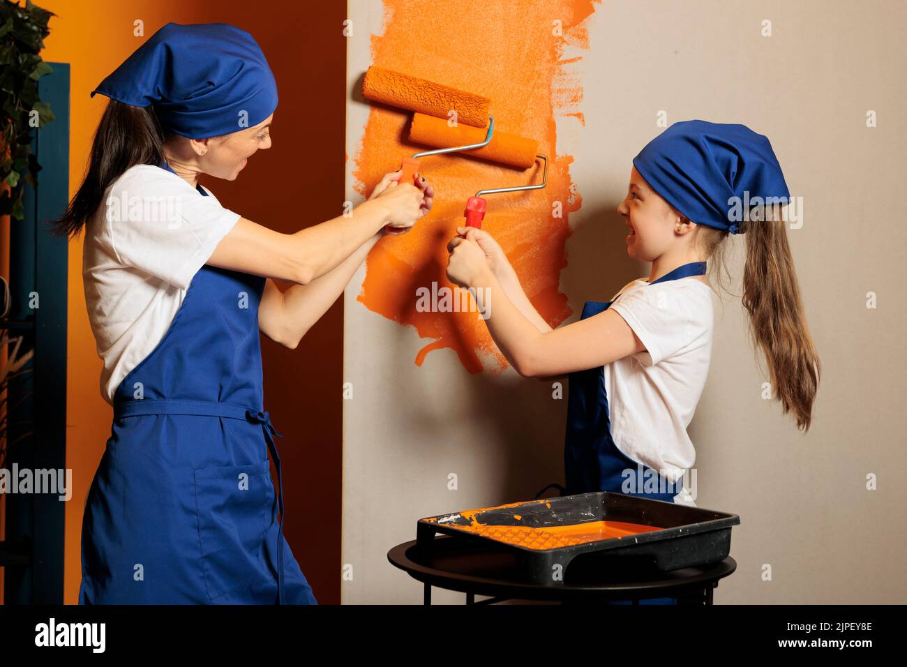 Woman and kid painting house walls with orange color paint, using ...