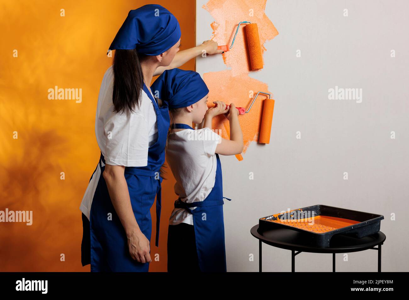 Small family painting walls with orange color paint and roller brush ...