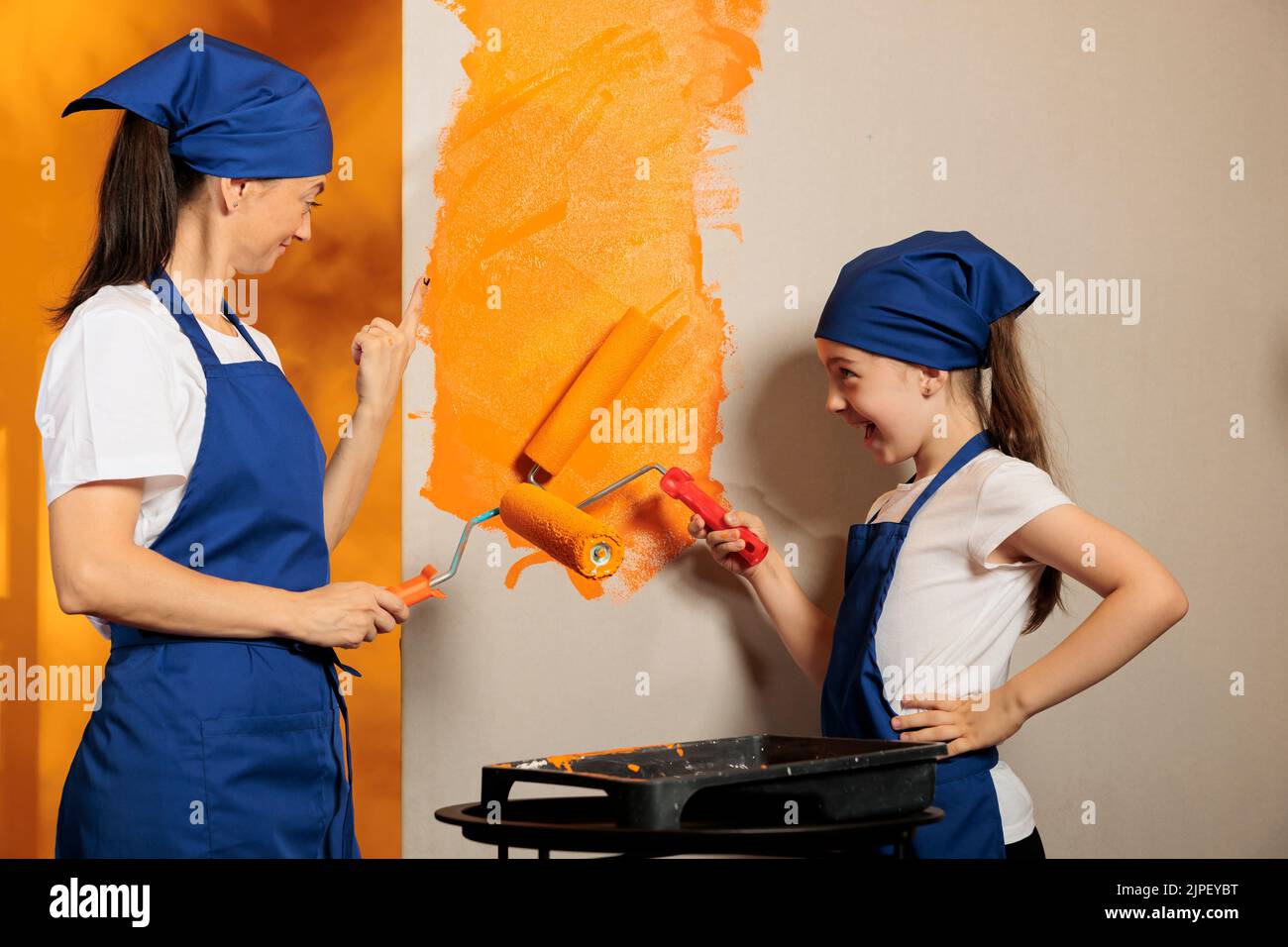 People having fun painting home walls, using orange paint color to ...