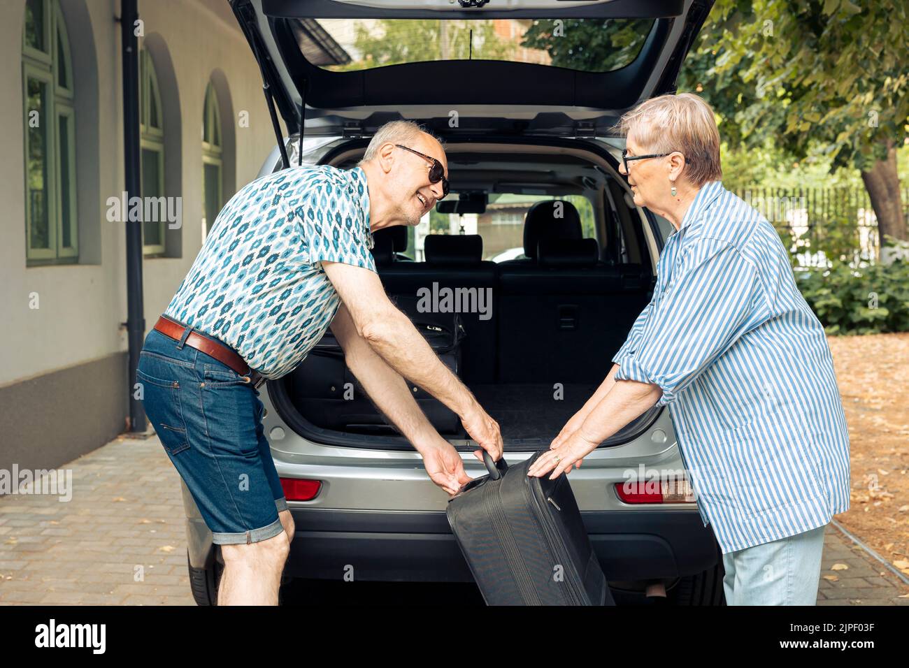 Senior people putting bags in vehicle trunk to leave on retirement ...