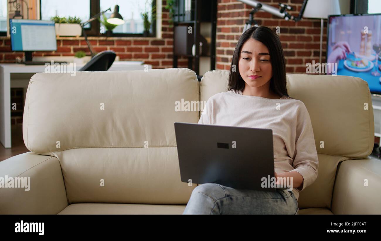 Focused woman sitting on sofa while working remotely on laptop ...