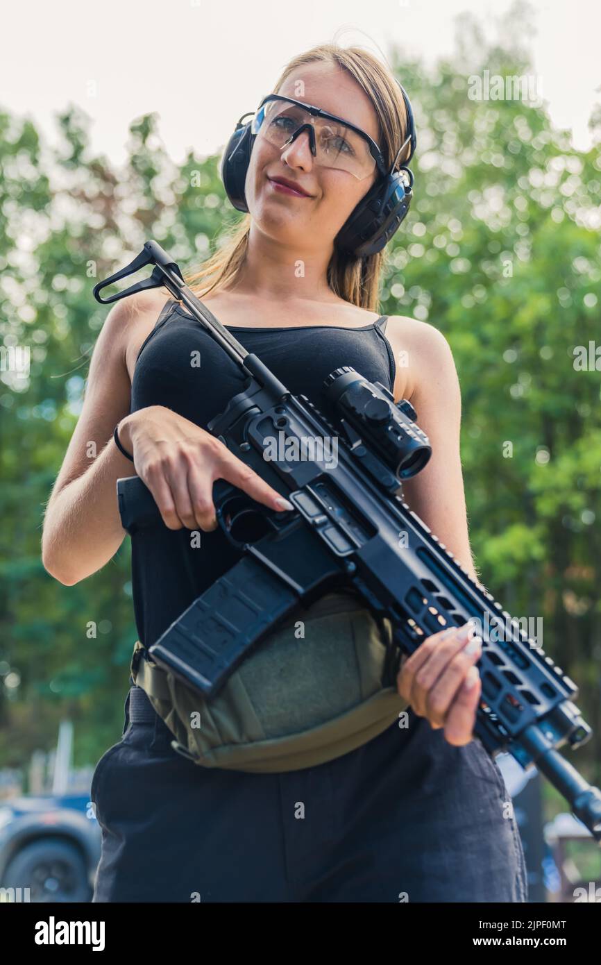 Young white woman wearing protective gear holding submachine gun ...