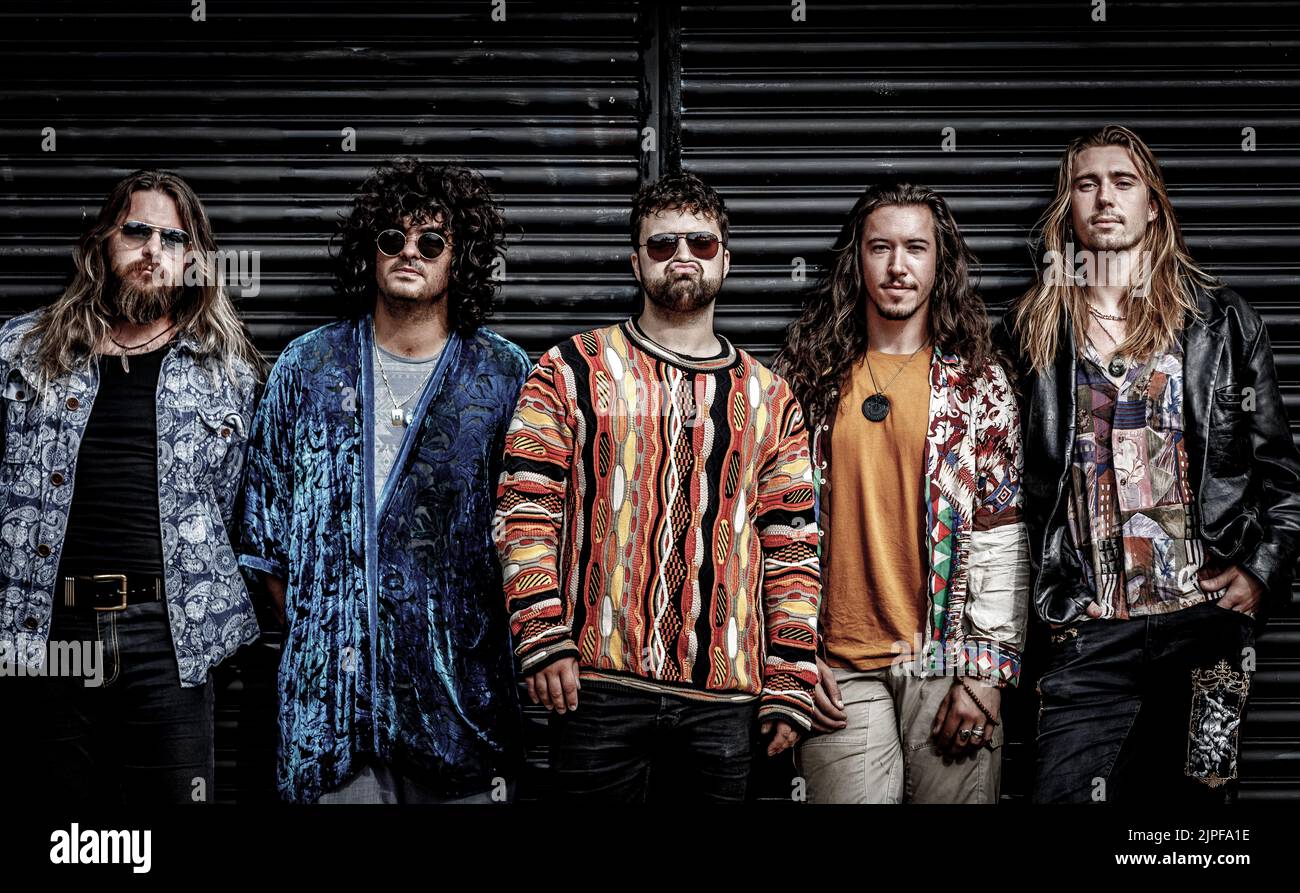 Five men in colorful clothes, stand posing against a dark metal ...