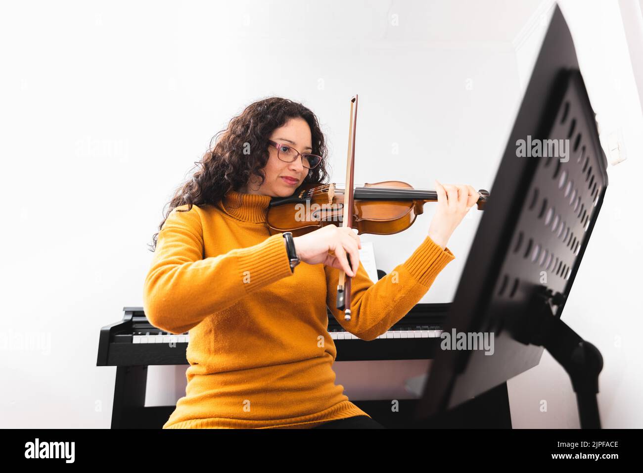 Brunette woman wearing a yellow sweater, and playing violin by reading ...