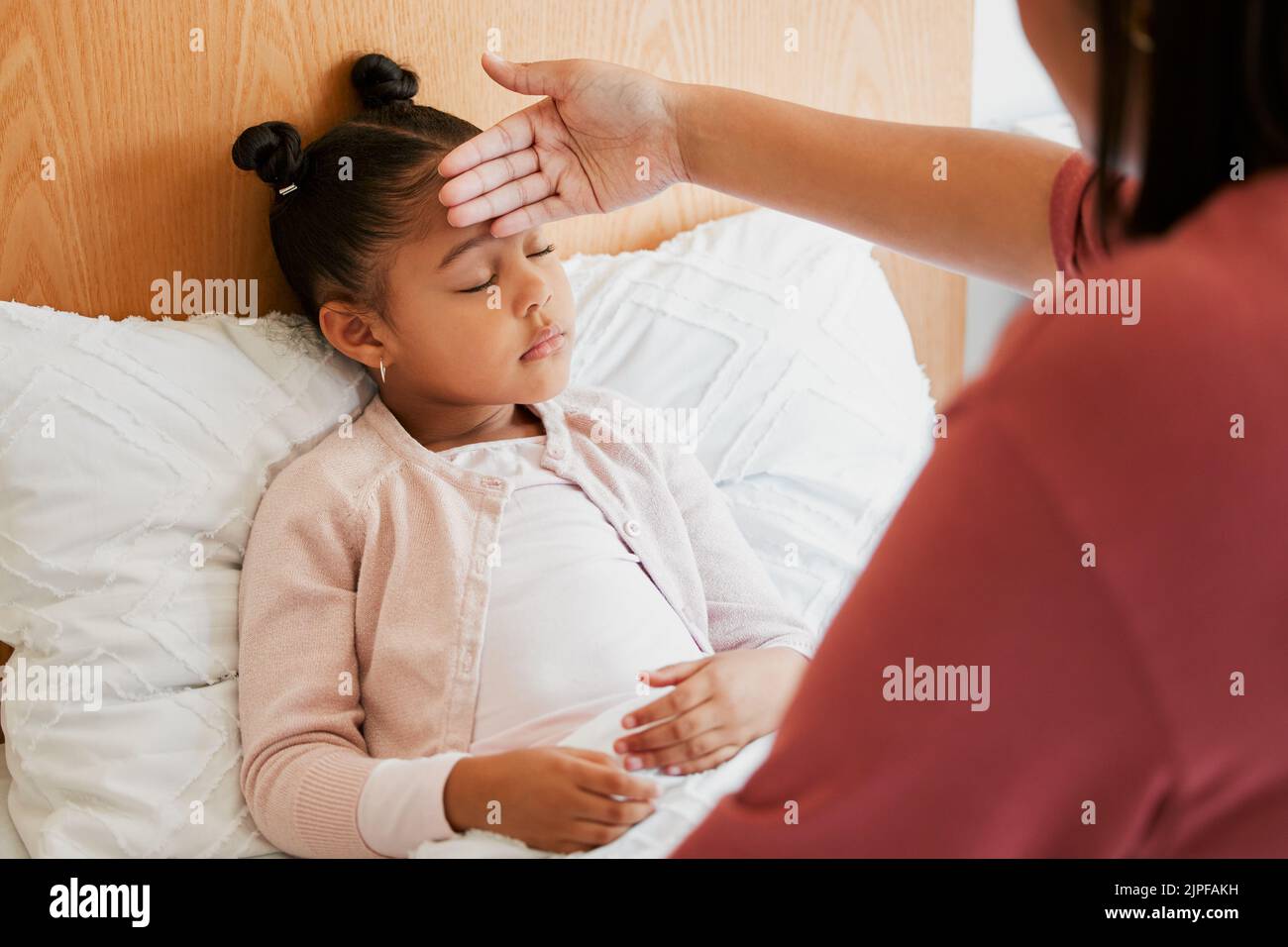 Sick child with mother checking forehead temperature, feeling ill and unwell. Small girl with ...