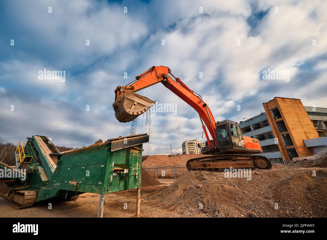 A construction excavator loads crushed stone into the receiving hopper ...