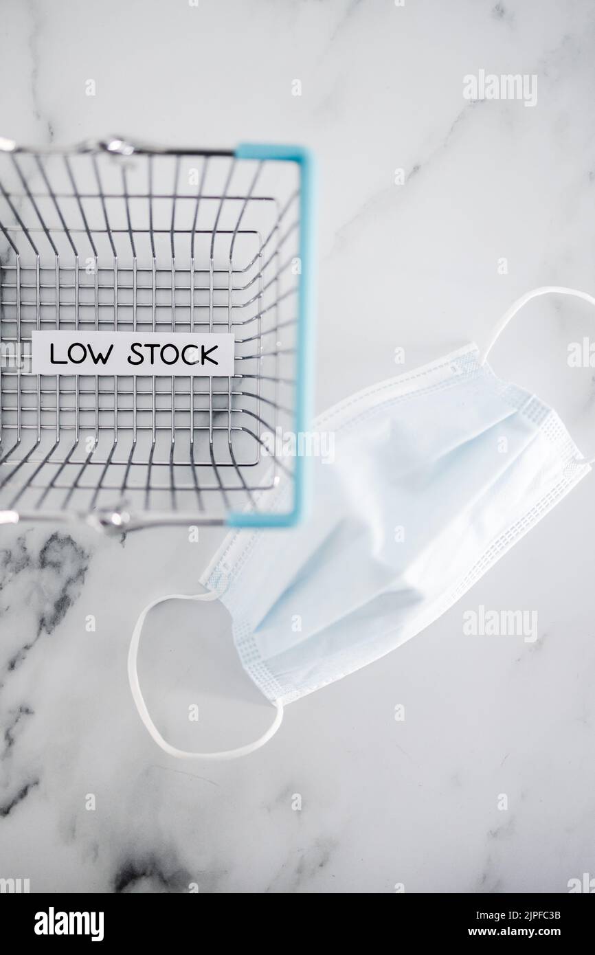 Low stock text in front of empty shopping basket with surgical mask on ...