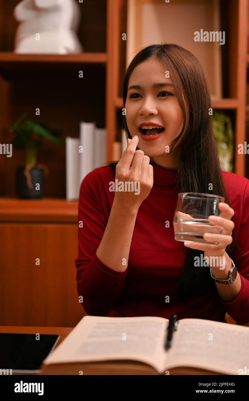 Beautiful young Asian businesswoman or female worker taking a vitamin ...