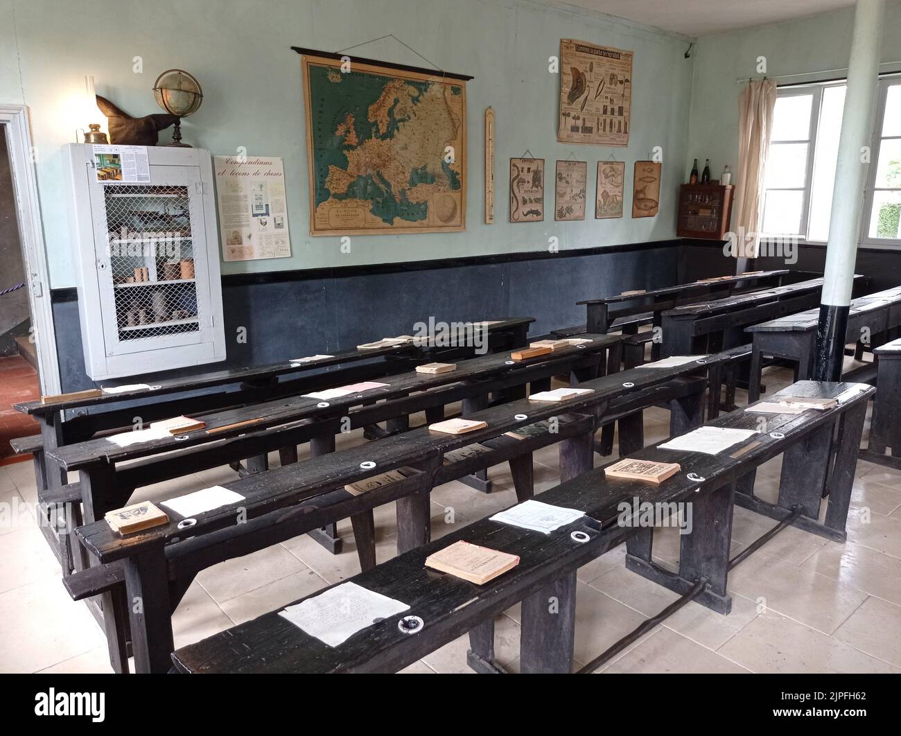 Une classe ancienne avec des bancs ,des affiches, des outils scolaires ...