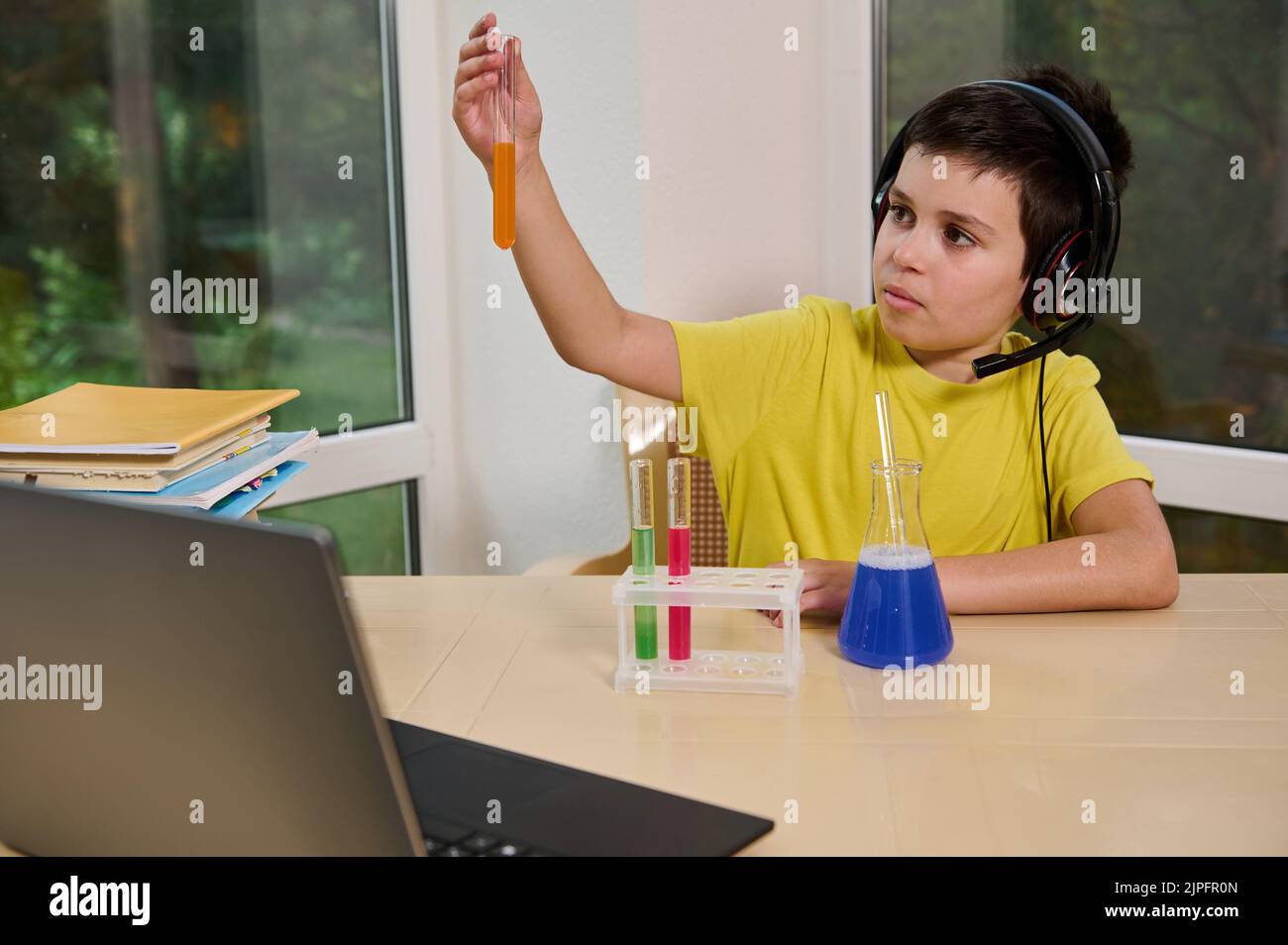 Inspired schoolboy conducting chemical experiment, holds a test tube ...