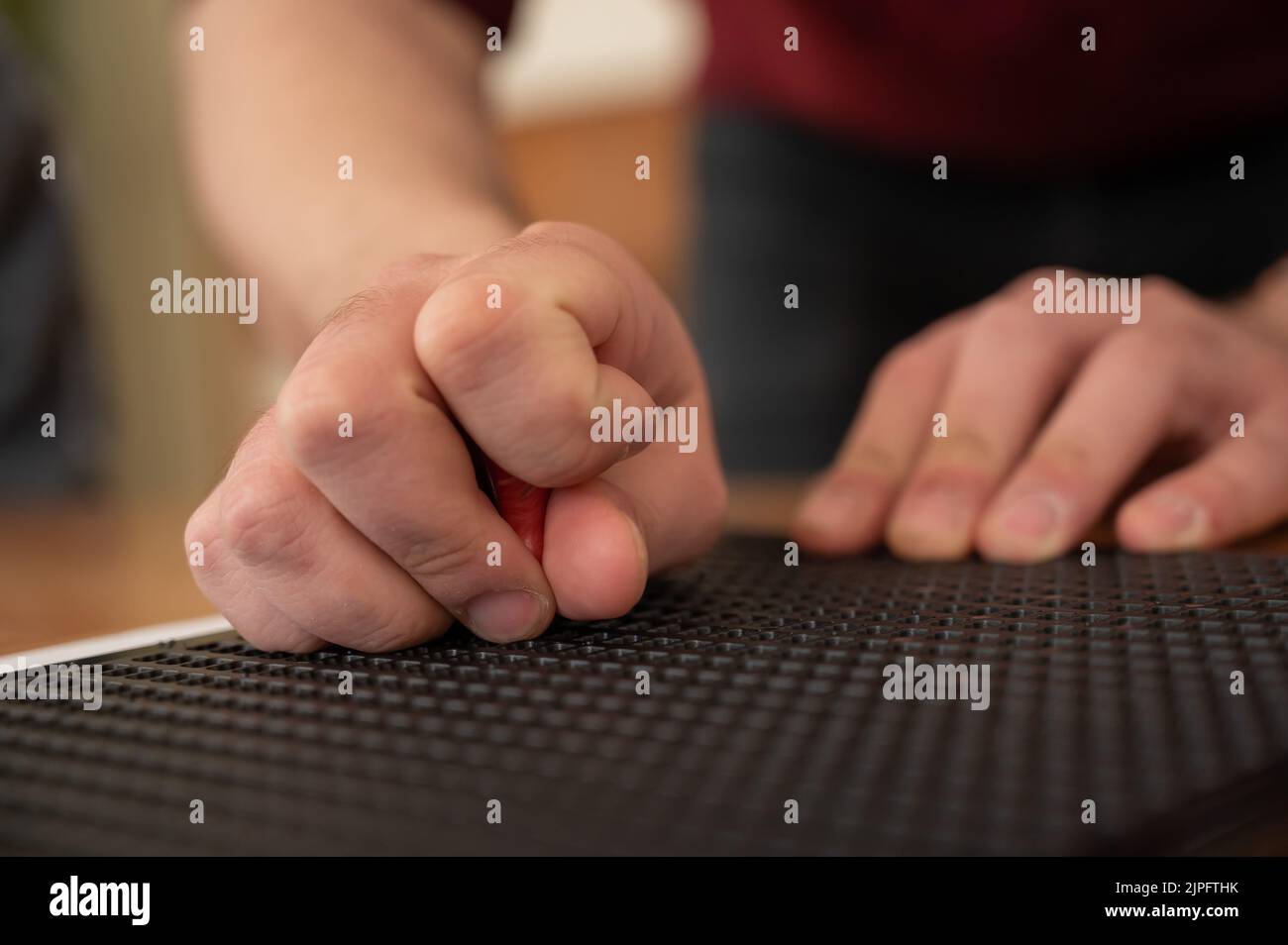 A man uses a special stencil and stylus to write a letter in braille ...