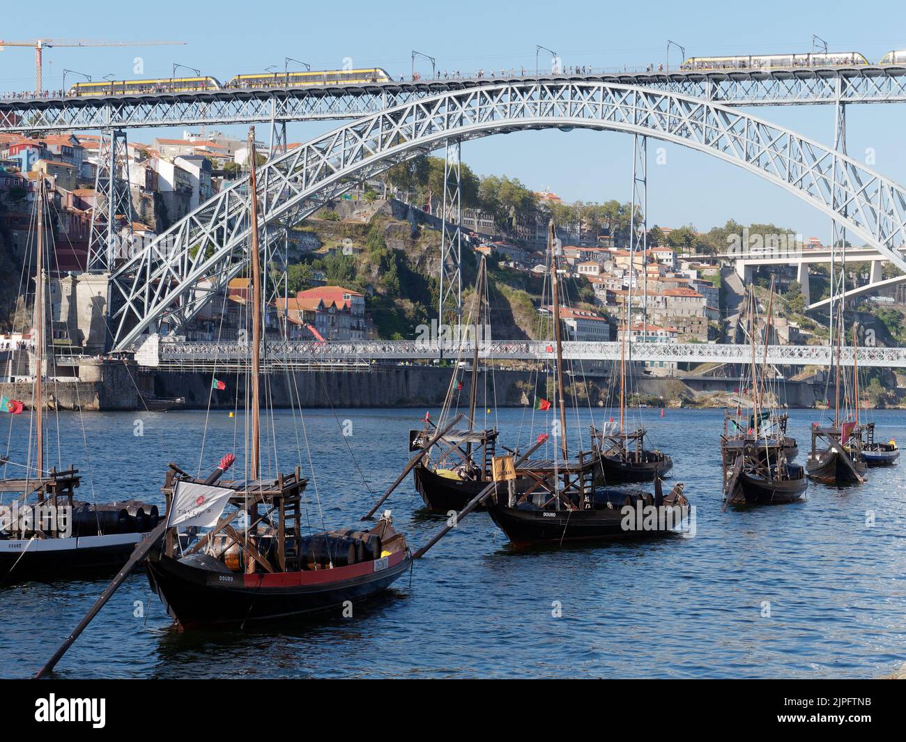 Traditional wine carrying boats on the River Douro. A metro train ...