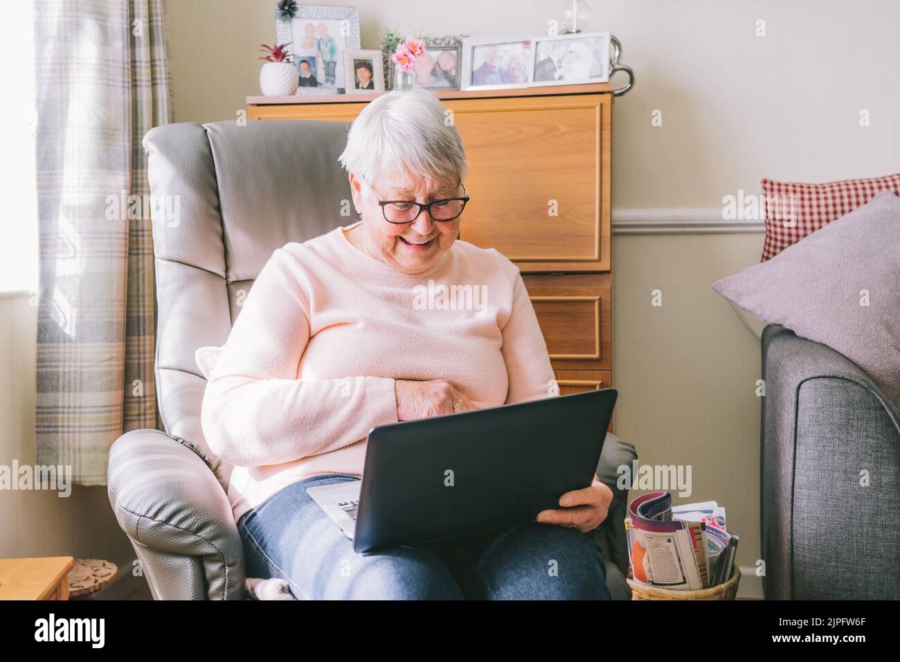 Senior grandmother sitting on armchair, looking at laptop screen. Grey ...