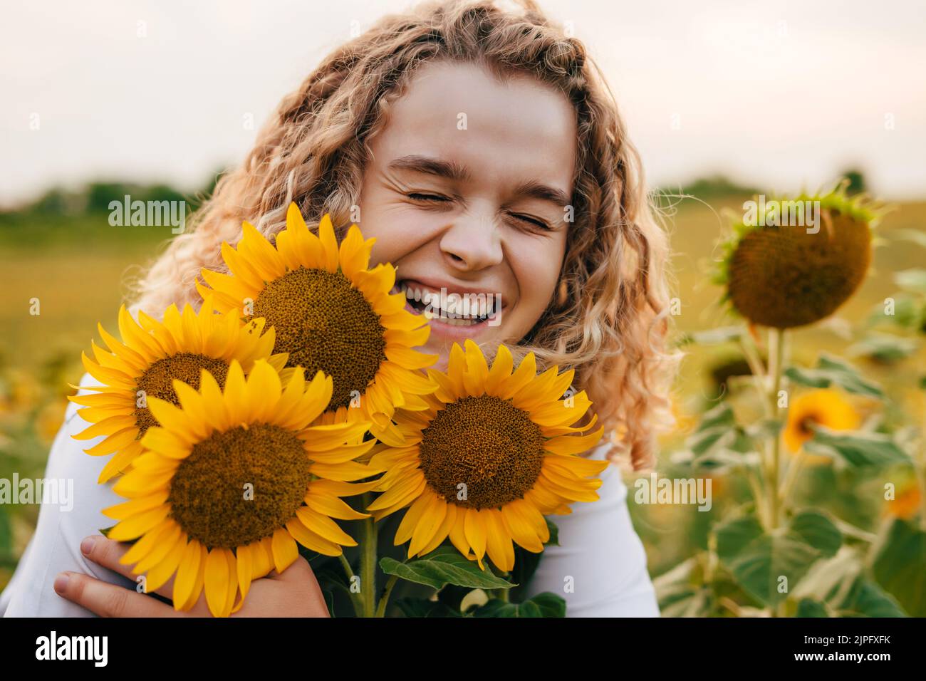 Happy curly girl embracing sunflower flowers in a field of sunflowers ...