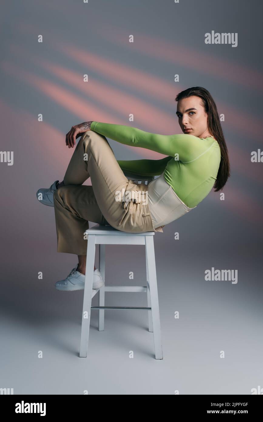 Stylish queer model posing on chair on abstract background Stock Photo ...