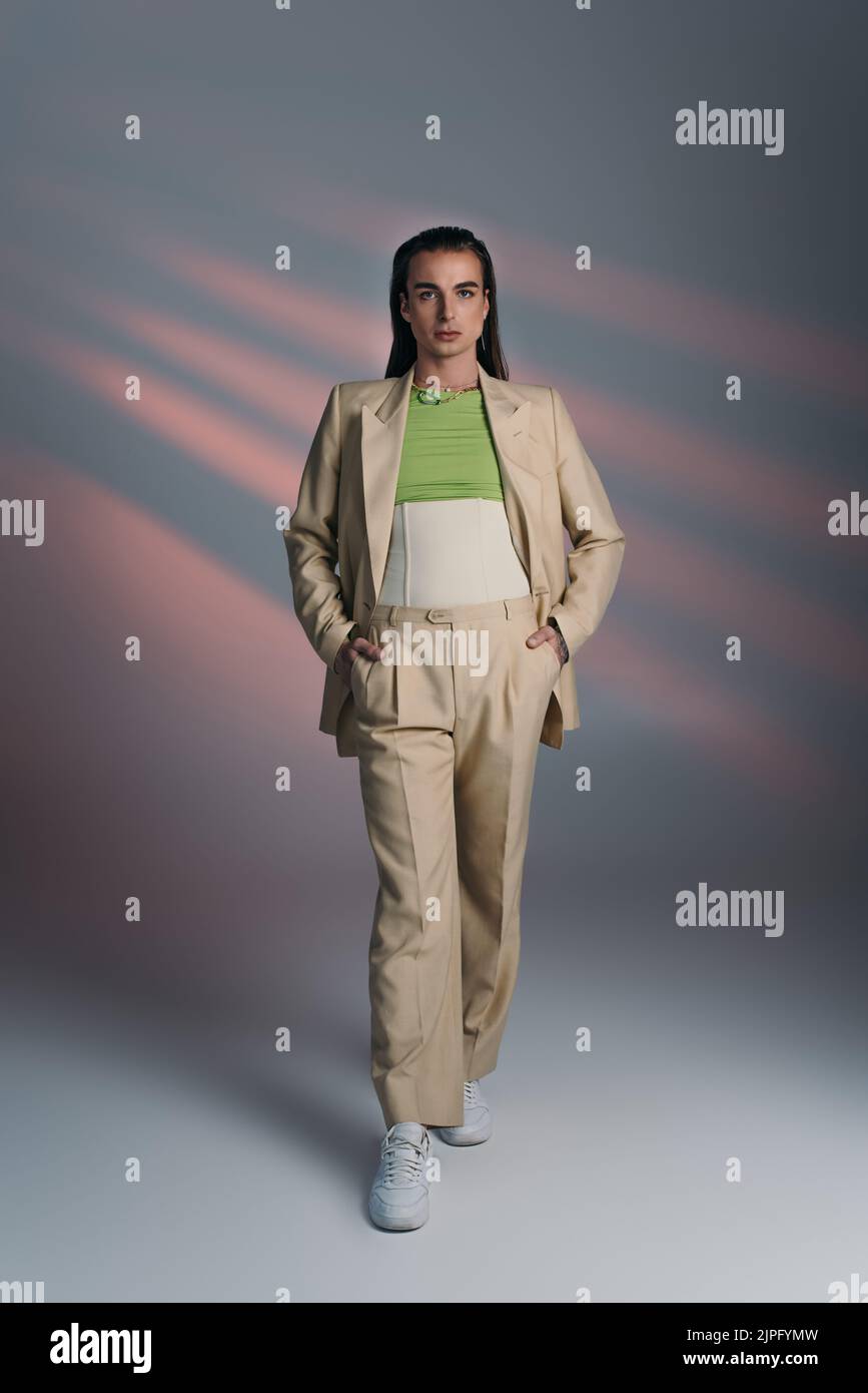 Full length of nonbinary model in suit and corset standing on abstract ...