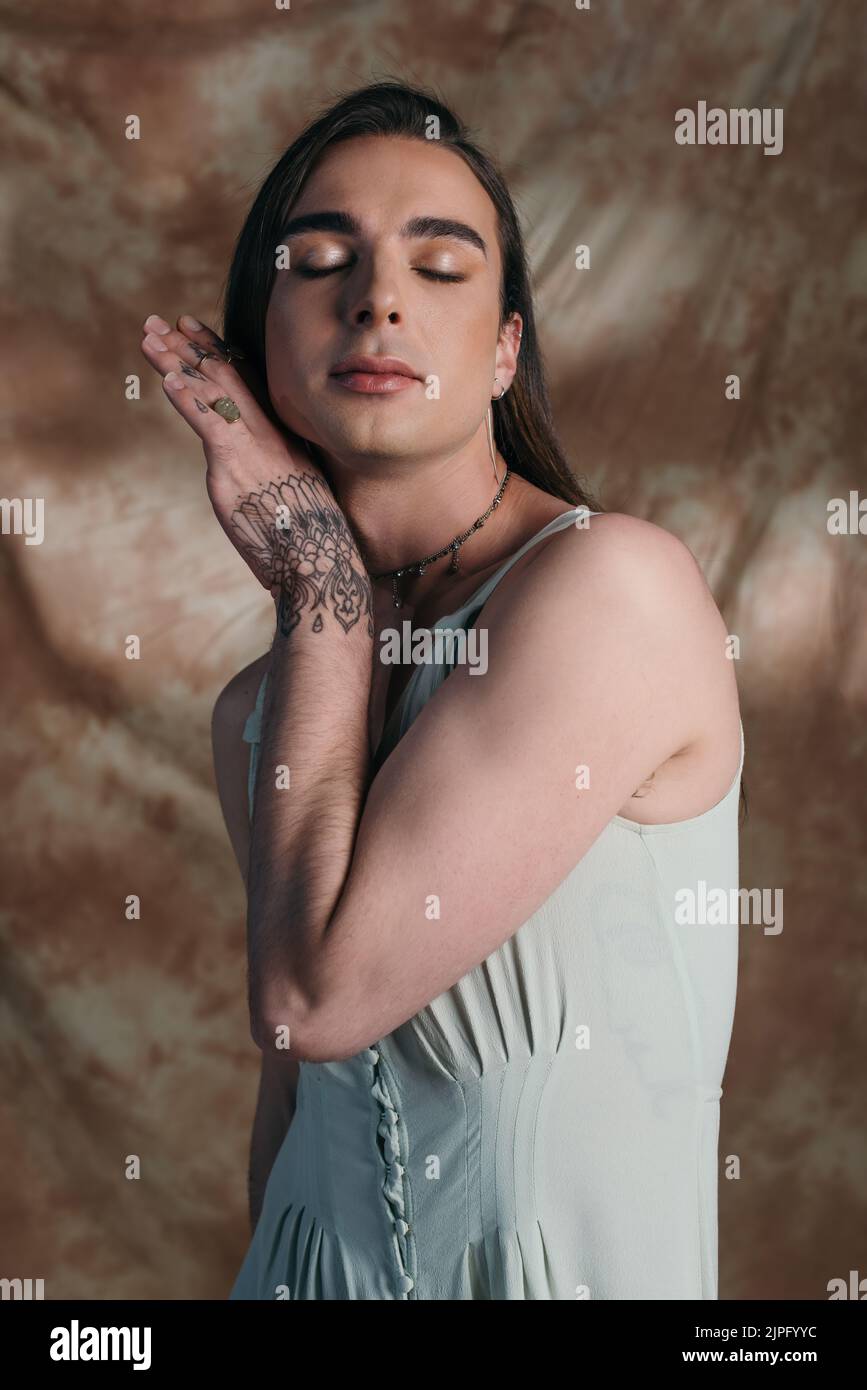Portrait of stylish queer person in dress posing on abstract brown ...
