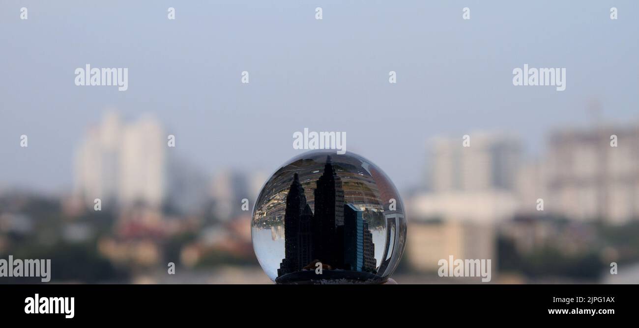 Toy skyscrapers inside a glass ball against a real city with soft focus ...