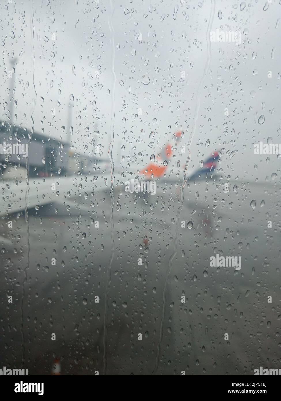 A plane window covered with rain drops looking at the wings of the ...