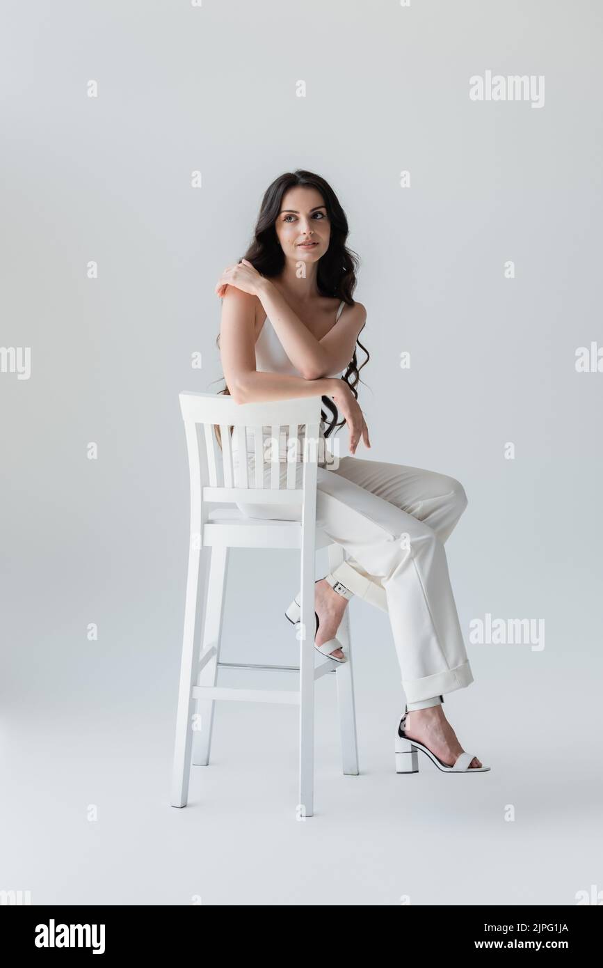 Full length of stylish woman touching shoulder while sitting on chair ...