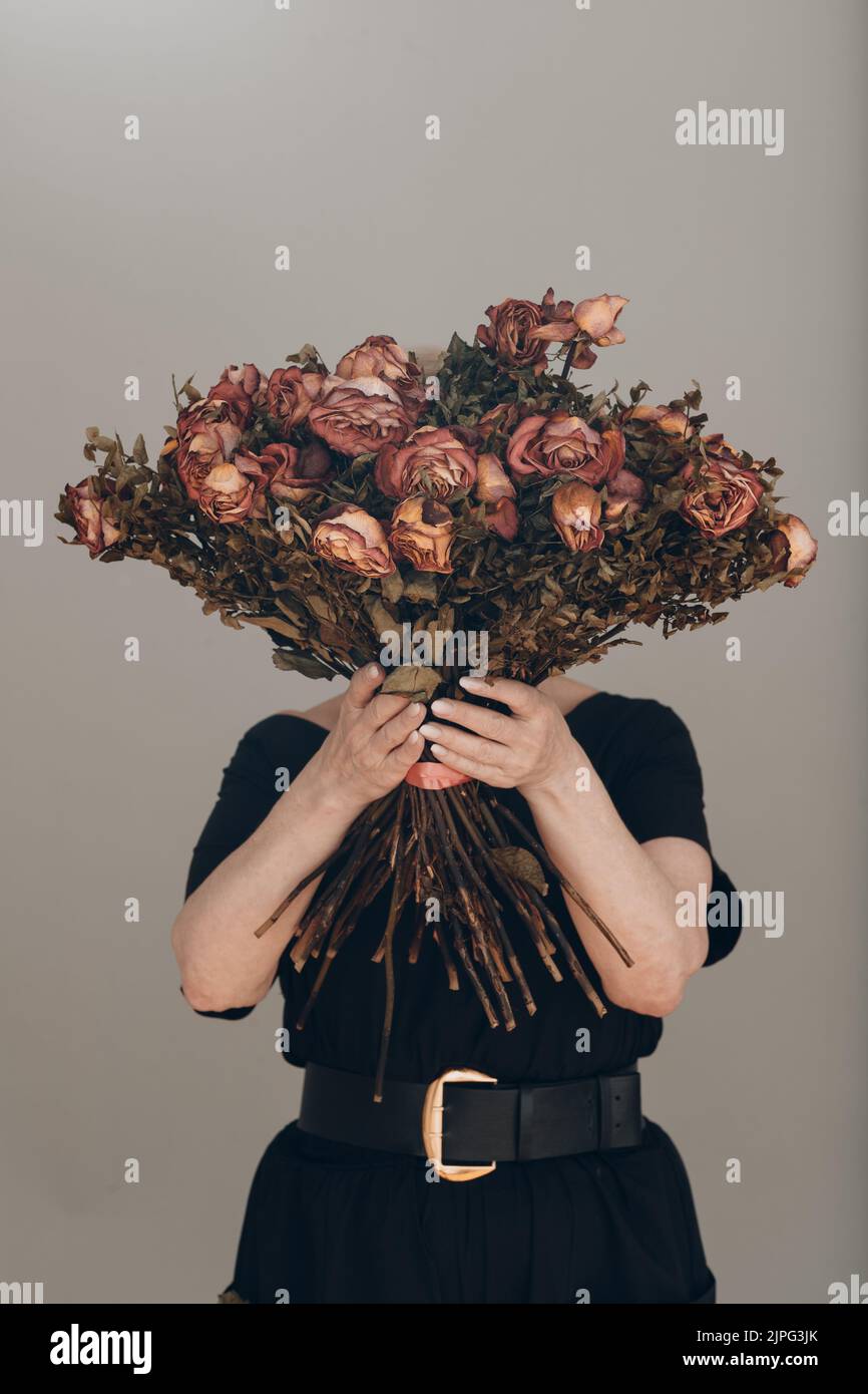 Upset elderly woman hold withered dry old rose flowers bouquet. Old age ...
