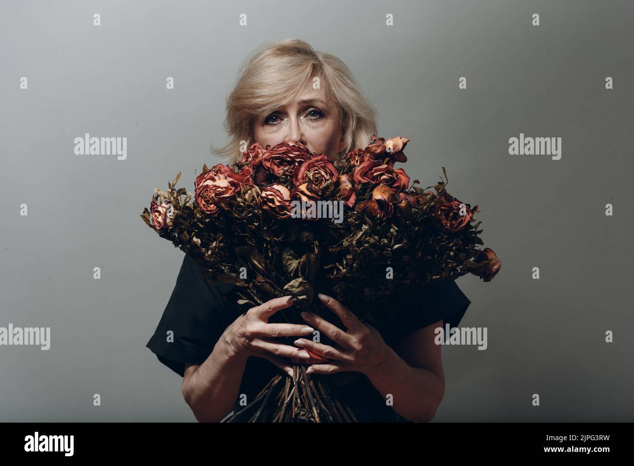 Upset elderly woman hold withered dry old rose flowers bouquet. Old age ...