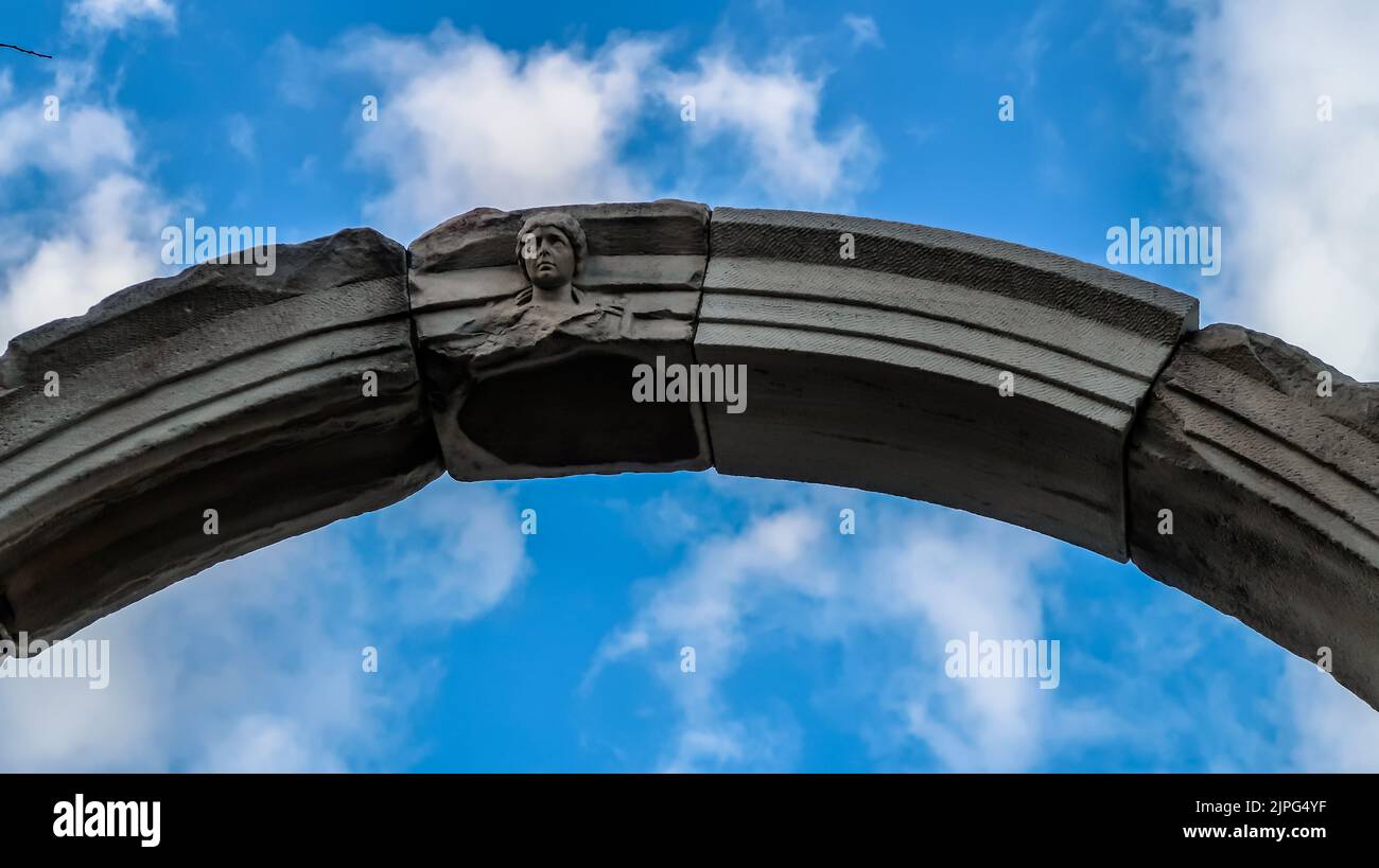Close up of arch structure with historical face on it and blue sky ...