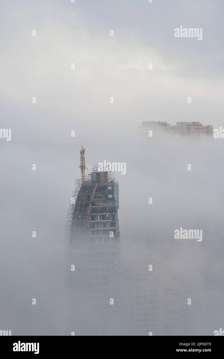 The top of a skyscraper under construction rises out of the fog in ...