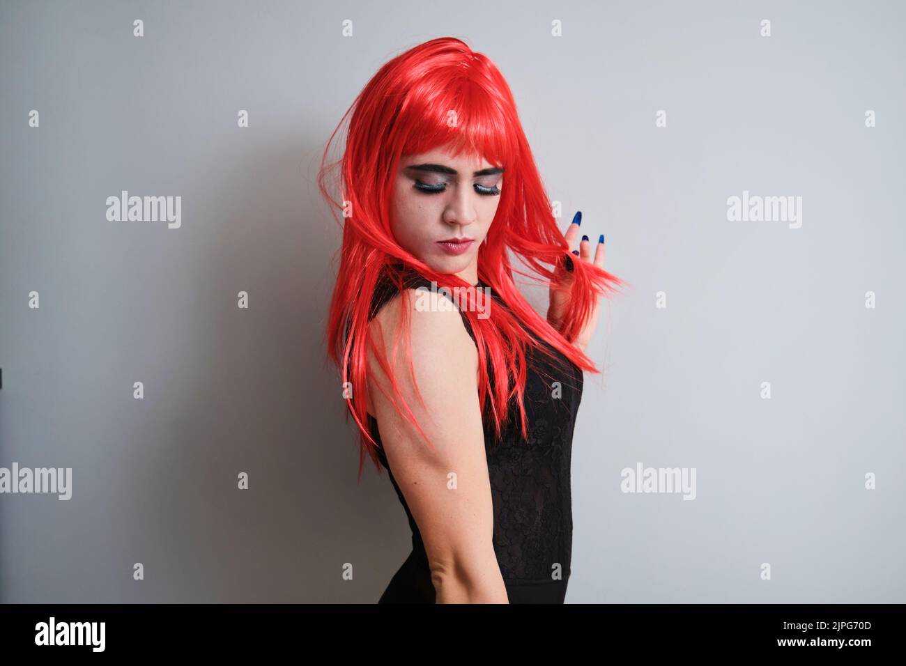 Portrait of transgender man looking down wearing a red wig on grey ...