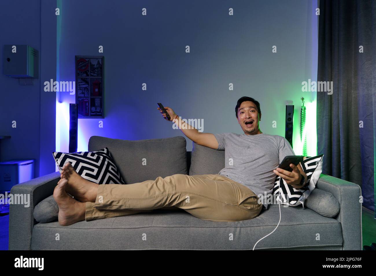 A young Southeast Asian male chilling and watching TV in the living ...