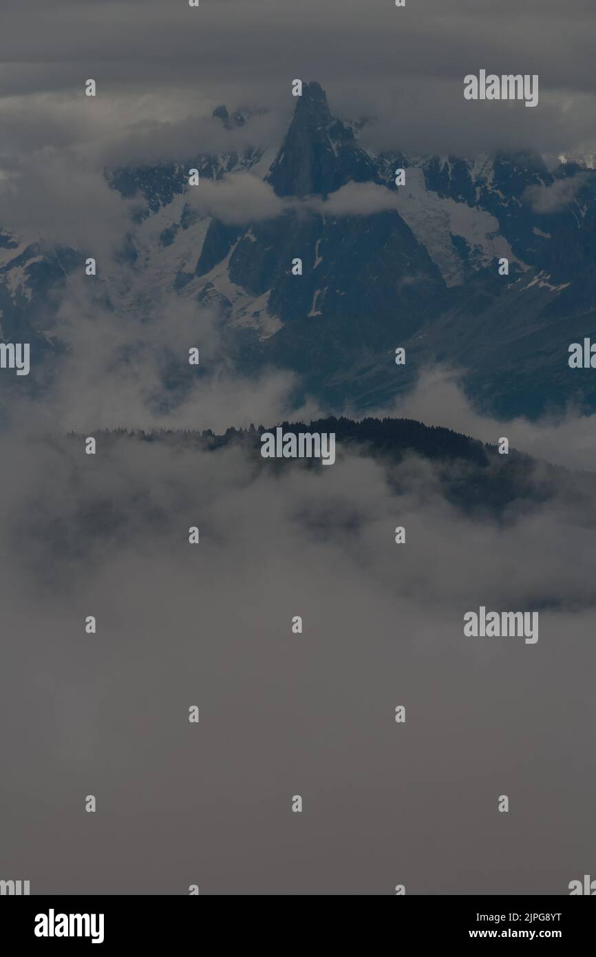 A vertical view of a mountain landscape covered in clouds in Alps ...