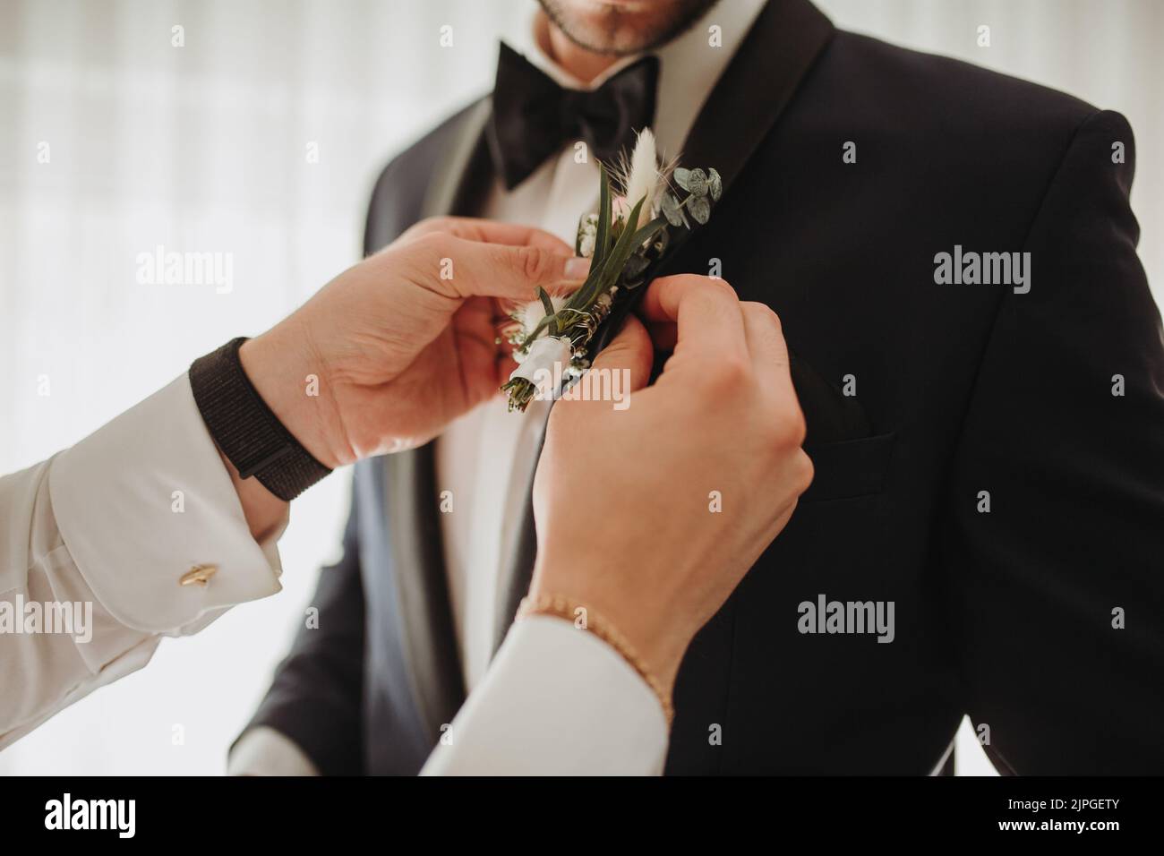 A closeup of male hands in white shirt attaching the floral buttonhole ...