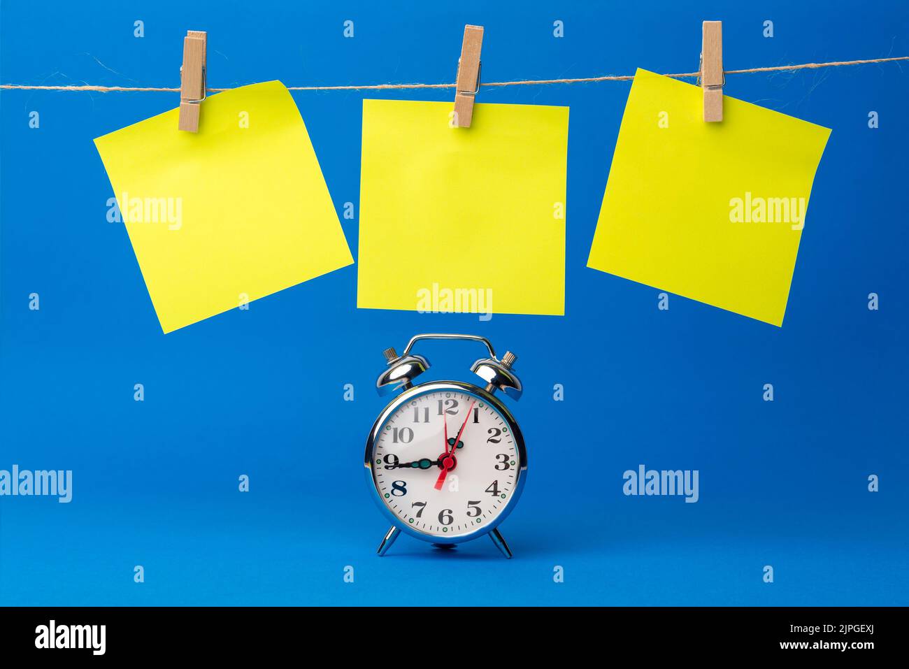 A clock next to a rope with yellow sticky notes hanging down to include ...